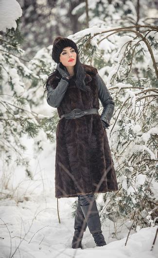 긴 검은 모피 코트와 숲에서 겨울 풍경을 즐기는 모자에 아름 다운 여자 눈 덮인 나무 아래에서 포즈를 취한 갈색 머리 소녀 숲에서 분기 밝은 추운 날에 매력적인 젊은 여자