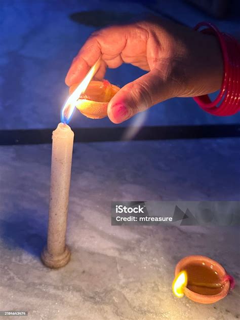 빨간 팔찌를 입고 알아볼 수 없는 여자의 클로즈업 이미지 촛불 불꽃 대리석 바닥에 서 있는 테이퍼 촛불에서 기름으로 가득 찬 조명 Mitti Clay Diya 어둠 속에서