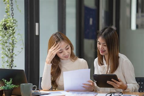 두 명의 젊은 아시아 여성 사업가가 새로운 스타트업 프로젝트 아이디어 프레젠테이션을 통해 이야기하고 상담하고 토론하고 사무실에서 마케팅 및 투자 계획을 분석합니다 2명에