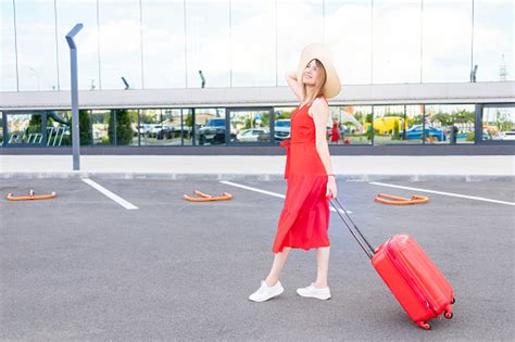 빨간 드레스와 모자를 쓴 공항에서 여행 가방을 든 행복한 소녀는 여름에 여행이나 휴가를 떠납니다 30 34세에 대한 스톡 사진