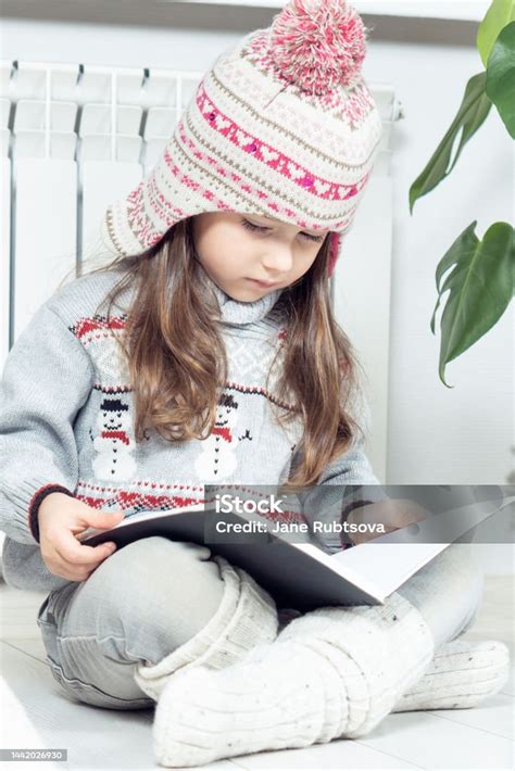 수직 집중 심각한 호기심 귀여운 어린 소녀 모직 모자 따뜻한 옷 눈사람 읽기 책 라디에이터 근처 4 5세에 대한 스톡 사진 및 기타 이미지 Istock