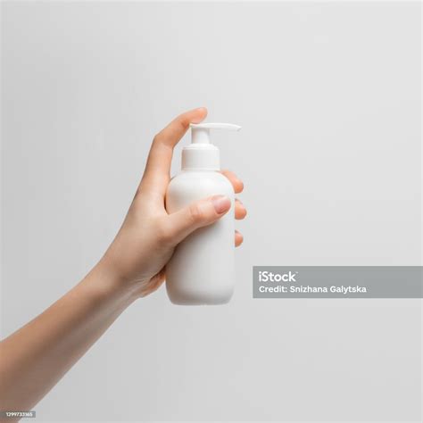 가벼운 배경에 여성의 손에 액체 핸드 크림 한 병 디스펜서가 있는 화이트 병 잘 손질된 손 자연스러운 짧은 손톱 건강관리와