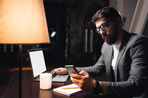 스마트폰 및 노트북 Coworking 스튜디오에서 사용 하는 사업 영 현대 로프트 사무실에서 밤에 새로운 시작에 대해 작업 하는 남자 수염 필름 효과 경영자에 대한 스톡