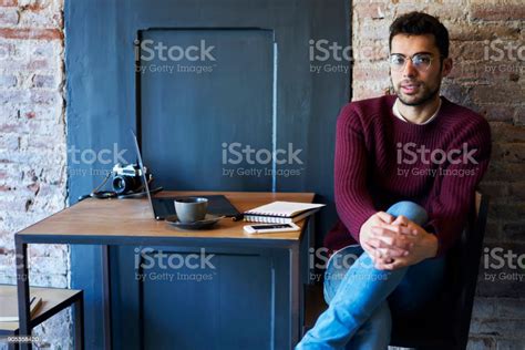 노트북 컴퓨터와 빈티지 카메라와 함께 테이블에 세련 된 커피숍에 앉아 광 안경에 남성 기자의 전체 길이 초상화 Hipster