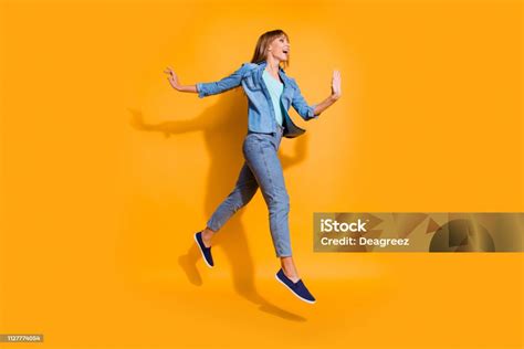 전체 길이 몸 크기 사진 비행 높은 점프에 놀라운 이빨 미소 아름 다운 노란색 배경에 고립 된 그녀가 숙 녀 건강 한 라이프 스타일 캐주얼 청바지 데님 셔츠 옷 입고 조깅