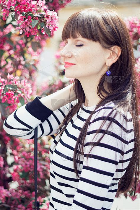 一位年轻女子站在一棵开花的树后面。
