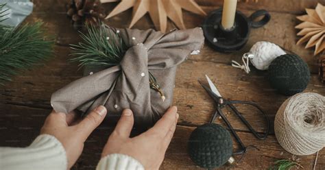 장식품이 있는 소박한 나무 테이블에 현대적인 축제 패브릭으로 포장된 크리스마스 선물을 들고 있는 손 분위기 있는 분위기 있는 이미지 북유럽 스타일 즐거운 성탄절