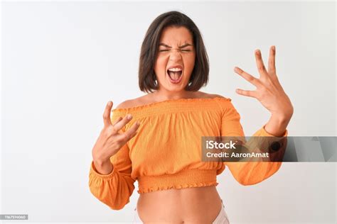 고립된 흰색 배경 위에 서있는 주황색 티셔츠를 입은 젊은 아름다운 여성은 팔을 들고 눈을 감고 흥분을 일으키며 성공을 축하하기