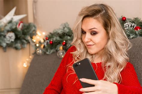 온라인 크리스마스 인사말 빨간색 스웨터를 입은 여성은 스마트폰을 사용하여 친구 부모 온라인 쇼핑을 통해 화상 통화를 합니다