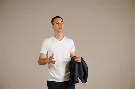 흰색 티셔츠를 입은 짧은 헤어스타일을 가진 젊고 어른스러운 검은 머리의 남자가 스튜디오에서 가벼운 배경을 가진 감정적으로 포즈를