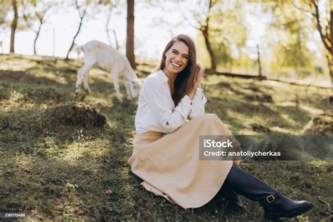 시골에서 따뜻한 가을 날에 풀을 뜯는 염소와 함께 햇볕이 잘 드는 목초지에 앉아있는 웃는 여자 20 24세에 대한 스톡 사진 및 기타 이미지 Istock