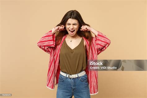 스튜디오에서 파스텔 베이 지 배경에 고립 된 손가락으로 귀를 덮고 카메라를 찾고 캐주얼에 미친 젊은 여자를 비명 사람들은 진심으로 감정 라이프 스타일 개념입니다 복사 공간을