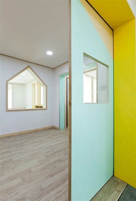 어린이집 민트와 옐로우 색상 포인트의 네모난 창이 달린 캐주얼한 문과 화이트 바탕에 우드톤 프레임의 지붕 모양 창이 어우러진 실내 사진