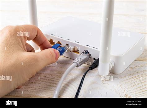 Woman Hand Plugging A Blue Network Cable Into Socket Of A White Wi Fi Wireless Router On A White