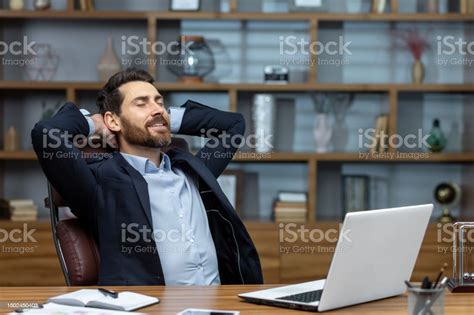 완성 작업 중요한 프로젝트 노트북을 사용하여 현대 사무실 건물 내부에서 일하는 성숙한 남자 수염과 안경을 가진 고위 상사가 머리 뒤에 손을 얹고 꿈을 꾸고 미래 계획을