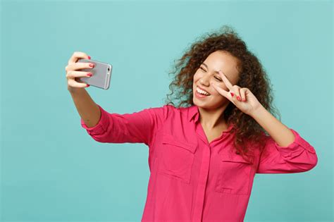 캐주얼에 쾌활 한 아프리카 소녀는 승리의 기호를 Shwoing 파란색 청록색 배경에 고립 된 휴대 전화에서 Selfie 샷을 하 고 사람들은 진심으로 감정 라이프 스타일