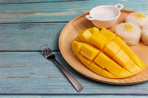 작은 포크와 노란색 반 망고 블루 나무 테이블에 망고 과일 큐브 열대 과일 아시아 신선한 노란 망고 껍질과 나무 정육점에 슬라이스 큐브 디저트 과일 열대 과일 여름 개념