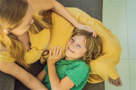 A Heartwarming Moment Pregnant Mother And Her Older Son Sit On The Sofa Engaging In A Tender