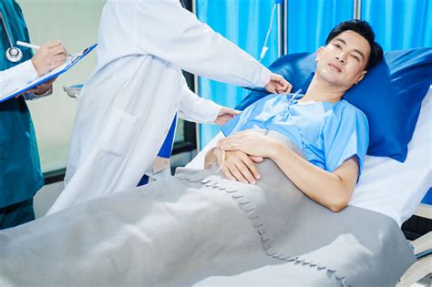 두 명의 무슬림 여성 의사가 병원에서 수술 후 침대에 누워 있는 남성 환자의 병력과 증상을 확인하고 회복 및 건강 상태를 모니터링합니다 3 명에 대한 스톡 사진 및 기타