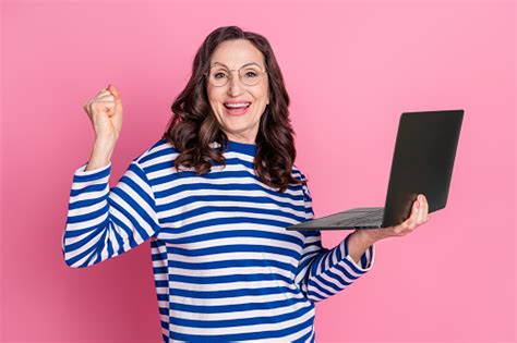 줄무늬 상의를 입고 노트북을 들고 분홍색 배경에서 성공을 축하하는 미소 짓는 성숙한 여자 65 69세에 대한 스톡 사진 및 기타 이미지 65 69세 갈색 머리