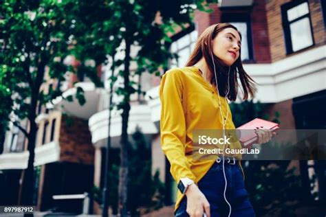 화려한 젊은 빨강 머리 여자 유행 브랜드 도시 주위를 산책 하 고 이어폰을 통해 음악을 듣고 의류 입고 현대 장치 및 메모장와 아름 다운 여자 학생 Mp3 플레이어에 대한