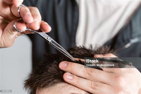 금속 가위로 머리를 자르는 클로즈업 마스터는 이발소에서 남자의 머리와 수염을 잘라 미용사는 젊은 남자를위한 헤어 스타일을 만든다