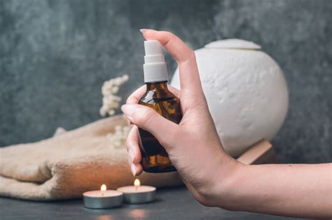 어두운 회색 배경에 여성의 손에 화장품 어두운 호박색 유리 병 클로즈업 카피스페이스 스파 양초와 꽃이 있는 어두운 유리 용기 향수 스프레이 살롱 트리트먼트 컨셉 미니멀리즘