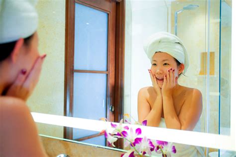 젊은 행복 하 고 아름 다운 아시아 한국 여자 집에서 또는 명랑 하 고 여성의 아름다움과 피부 관리에서 자연 스러운 메이크업을 적용 하는 화장실 수건에 싸여 호텔 욕실의