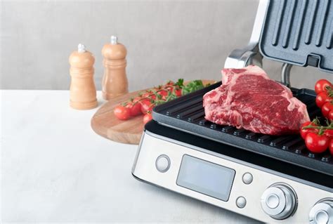 전기 그릴에 있는 원시 프라임 스테이크 블랙 앵거스 프라임 고기 스테이크 로즈마리 체리 토마토와 후추를 곁들인 현대적인 전기 그릴에 있는 Ribeye 현대적인 주방에서 요리