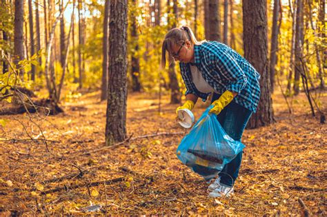 한 여성 환경 보호론자가 숲에서 쓰레기를 수거하고 있다 파란 쓰레기 봉투를 손에 든 여성이 숲에서 플라스틱 쓰레기를 모으고 있다 한 여성이 쓰레기로 오염된 숲을 구합니다 2