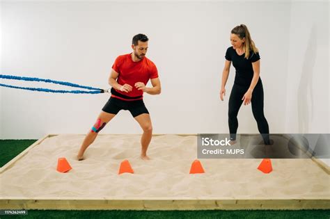 남자는 허리에 파란색 지원으로 모래에 스트레칭 운동을수행 물리 치료사 소녀 배경에 흰색 벽에 의해 지원 근육 건강과 이완의 개념 다채로운 사진 보디 빌딩에 대한 스톡 사진