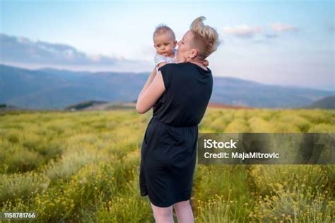 화창한 여름날 가족의 사랑과 성실 밝은 노란색 배경에 밝은 노란색 꽃밭에 서있는 작은 아기를 손에 들고있는 젊은 어머니의 초상화 가족에 대한 스톡 사진 및 기타 이미지