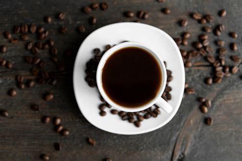 나무 테이블 배경에 구운 커피 콩커피 컵 나무 테이블에 흩어져 있는 커피 콩이 있는 검은 색 코프 잔 신선한 커피 콩 갈색에