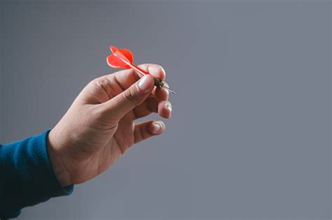 빨간 다트를 들고 있는 손이 클로즈업되어 평범한 회색 배경에서 목표물을 명중할 준비가 되어 있습니다 정확성 집중 및 성공의 개념 개념에 대한 스톡 사진 및 기타 이미지