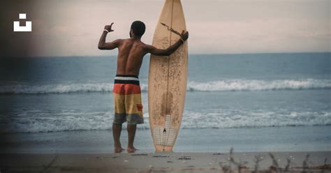 낮 동안 해변에서 갈색 서핑보드를 들고 있는 검은색 반바지를 입은 남자 사진 Unsplash의 무료 바다 이미지