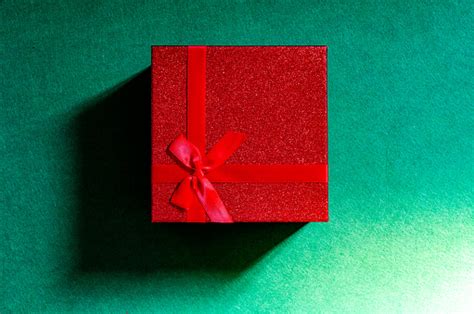 컴포지션 중앙에 고립된 밝은 리본이 있는 빨간색 선물 상자는 녹색 배경에 그림자와 볼륨을 만들고 아래쪽 여백에서 깜박입니다 12