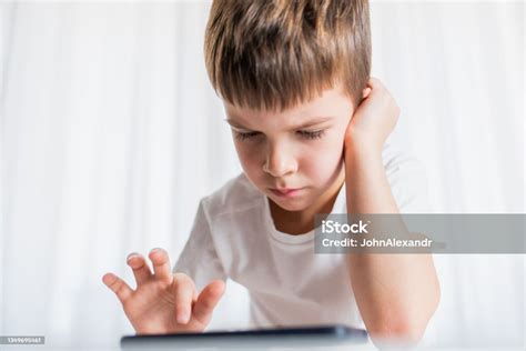 흰색 티셔츠를 입은 쾌활한 아이가 집에서 전화로 게임을 합니다 행복한 소년이 스마트폰을 본다 6 7 살에 대한 스톡 사진 및 기타 이미지 Istock