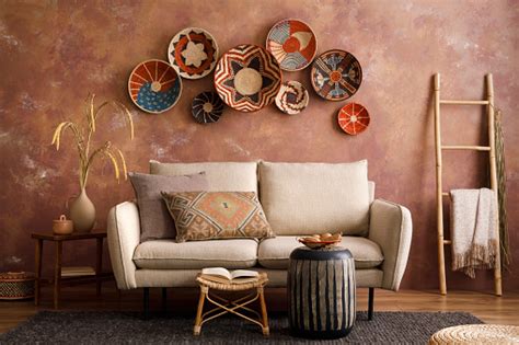 디자인 베이지 색 소파 커피 테이블 의자 고리 버들 바구니 및 개인 액세서리가있는 거실 인테리어의 세련된 보호 퇴비 갈색과 흰색 베개와 격자무늬 아늑한 아파트 가정 장식