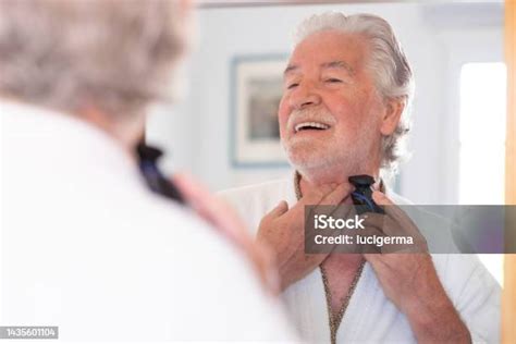 거울 앞에서 자신을 바라 보는 전기 면도기로 목욕 가운을 면도 수염을 깎는 잘 생긴 노인의 초상화를 닫으십시오 70 79세에 대한 스톡 사진 및 기타 이미지 Istock