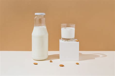 햇볕이 잘 드는 배경이 있는 흰색 나무 트레이에 병이 있는 아몬드 견과류의 비건 우유가 있는 유리 유제품 및 유당 무료 대체 음료 건강한 식품 성분 개념 트렌디 한 색상