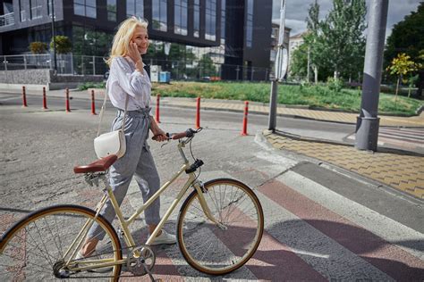 비즈니스 파트너와 휴대폰으로 통화하는 동안 손에 자전거를 들고 횡단보도를 걷고 있는 세련된 여성 사진 Unsplash의 유행 이미지