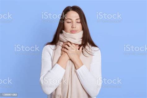 흰색 캐주얼 셔츠를 입은 젊은 여성이 스카프에 싸여 목이 아환하고 목에 손을 얹고 화가 났습니다 인후통 고통스러운 삼키기 푸른