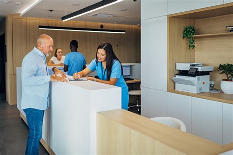 노인은 접수 데스크에 서서 의료 양식을 작성하는 방법을 설명하는 간호사의 말을 주의 깊게 듣습니다 25 29세에 대한 스톡 사진 및 기타 이미지 Istock