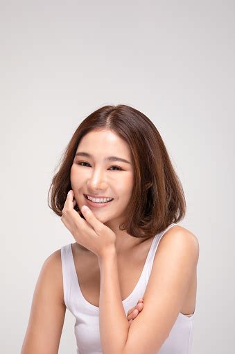 깨끗하고 신선한 피부 행복과 긍정적 인 감정과 명랑 회색 배경에 고립 된 아름다움과 화장품 개념으로 부드러운 뺨 미소를 만지는 아름다운 아시아 젊은 여성 건강관리와 의술에