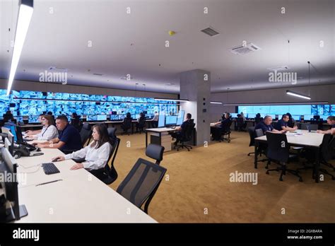 Group Of Security Data Center Operators Working In A CCTV Monitoring Room Looking On Multiple