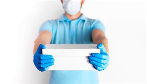 검역 기간 동안 물품 배달의 개념 2019ncov 의료용 마스크와 파란 장갑을 낀 젊은 남자는 하얀 바탕에 하얀 판지 상자를 손에 들고 있다 비접촉식 배송 바이러스 보호