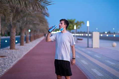 코로나바이러스 확산을 방지하고 안전하게 유지하기 위해 보호 수술 용 마스크를 착용하고 실행 트랙에 물병을 들고 남자를 적합 30 39세에 대한 스톡 사진 및 기타 이미지