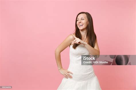 하얀 웨딩 드레스 서 포인팅 검지 손가락 보고 옆으로 파스텔 핑크 배경에 고립에서 즐거운 신부 여자 웃음의 초상화 결혼식 축 하 개념입니다 광고에 대 한 공간을 복사 합니다