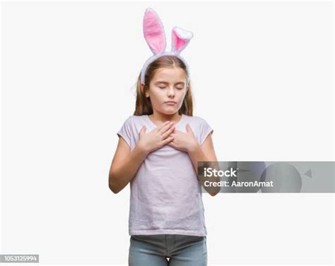 젊은 아름 다운 소녀와 함께 웃 고 고립 된 배경 위에 부활절 토끼 귀 입고 닫힌된 눈과 얼굴에 감사 제스처와 함께 가슴에 손 건강 개념입니다 아이에 대한 스톡 사진 및