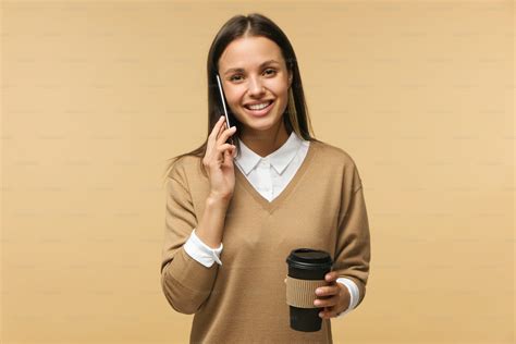 웃고 있는 젊은 여자가 전화로 이야기하고 테이크아웃 커피를 들고 있는 스튜디오 초상화 사진 Unsplash의 초상 이미지